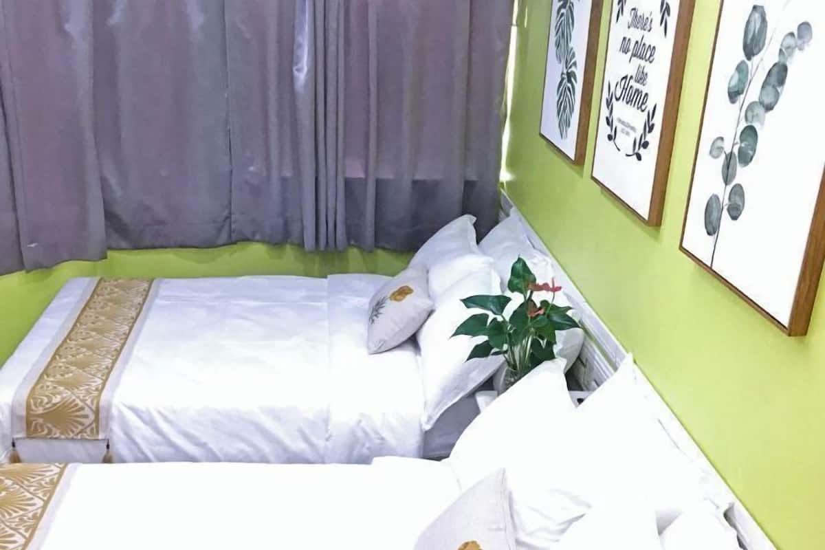 Quarto com duas camas de solteiro, parede verde e quadros.