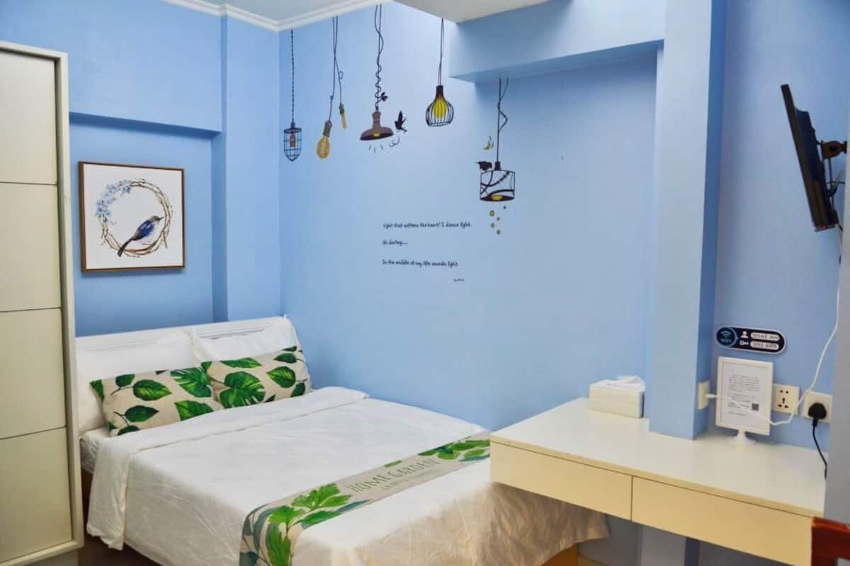 Quarto com cama, mesa de cabeceira, televisão na parede e uma obra de arte na parede.