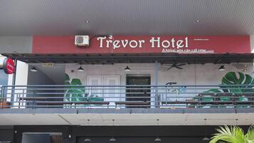 Exterior do Trevor Hotel, com toldo vermelho, placa de identificação e varanda com grades.