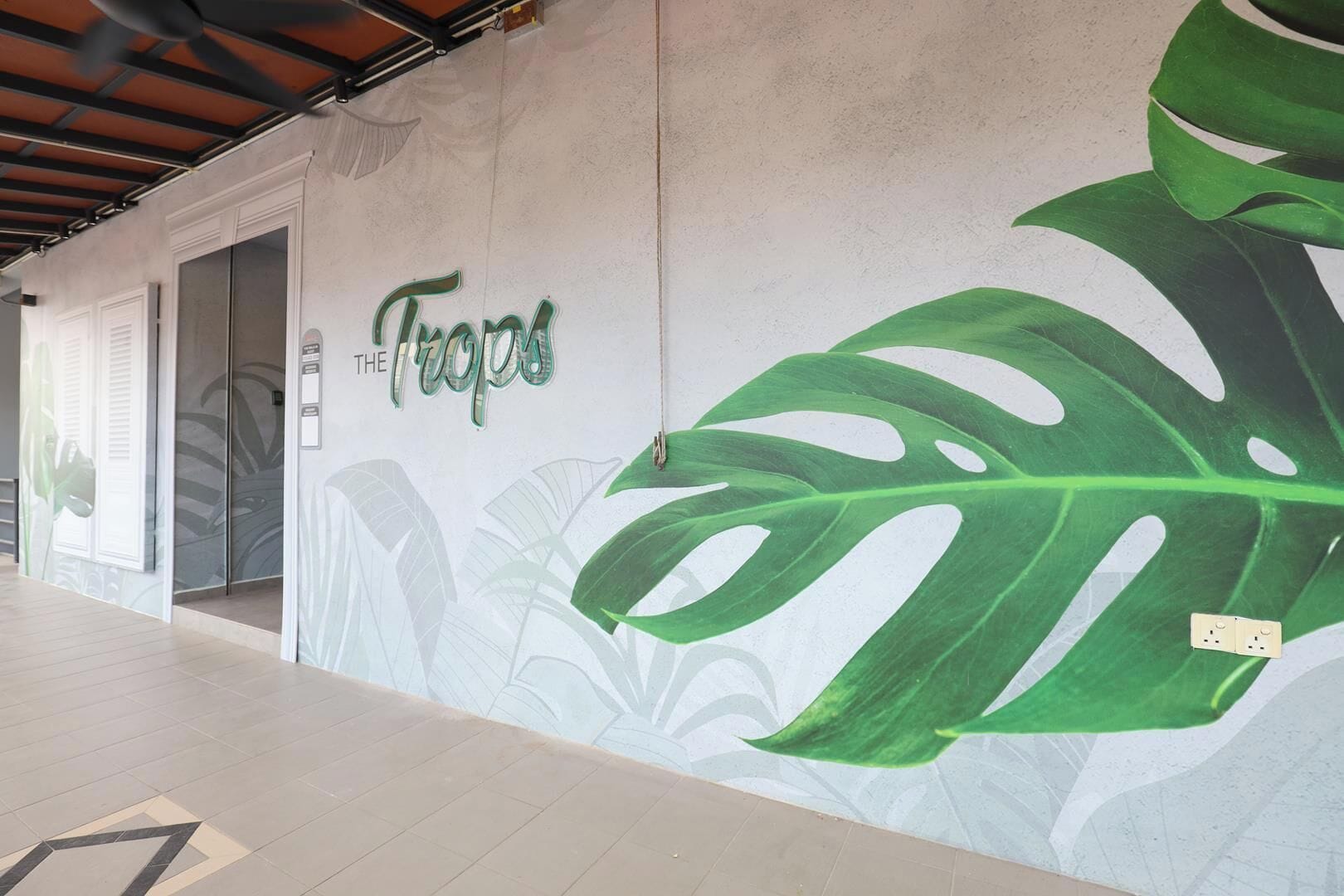 Corredor com um mural de folhas tropicais e a inscrição 'The Tropics' na parede.