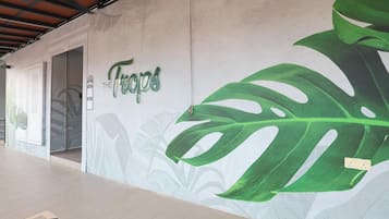 Corredor com um mural de folhas tropicais e a inscrição 'The Tropics' na parede.