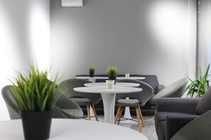 Uma área de estar moderna com mesas redondas, cadeiras estofadas cinzentas e pequenos vasos com plantas.