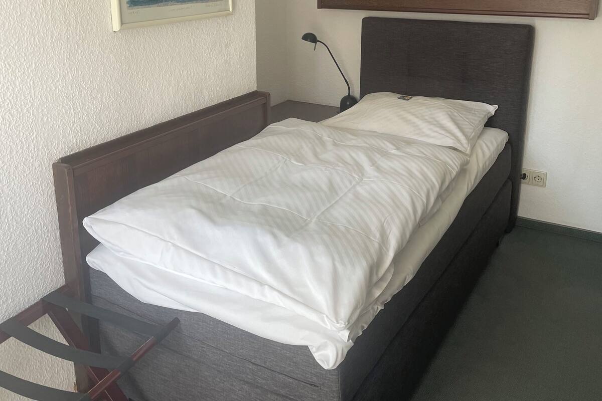 Uma cama de solteiro com cabeceira de madeira, uma mesa de cabeceira, um abajur e um quadro na parede.