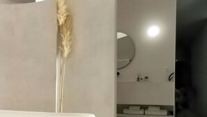 Quarto moderno com design minimalista, apresentando cama com roupa de cama branca, um espelho grande e capim-das-pampas decorativo.
