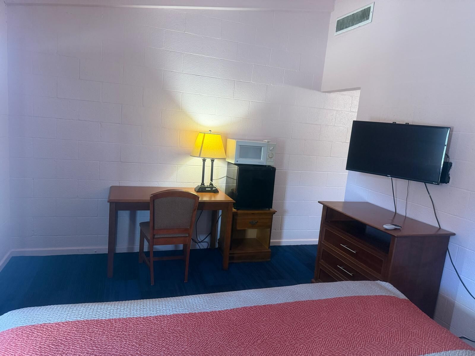 Quarto de hotel com cama, escrivaninha com cadeira, televisão, micro-ondas e cómoda.