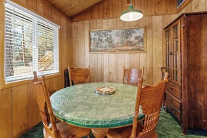 Um quarto com painéis de madeira, uma mesa de jantar, cadeiras, um armário e uma janela com persianas.