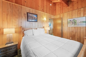 Quarto com painéis de madeira, uma cama grande, duas luminárias de cabeceira, um penteado e duas molduras na parede.