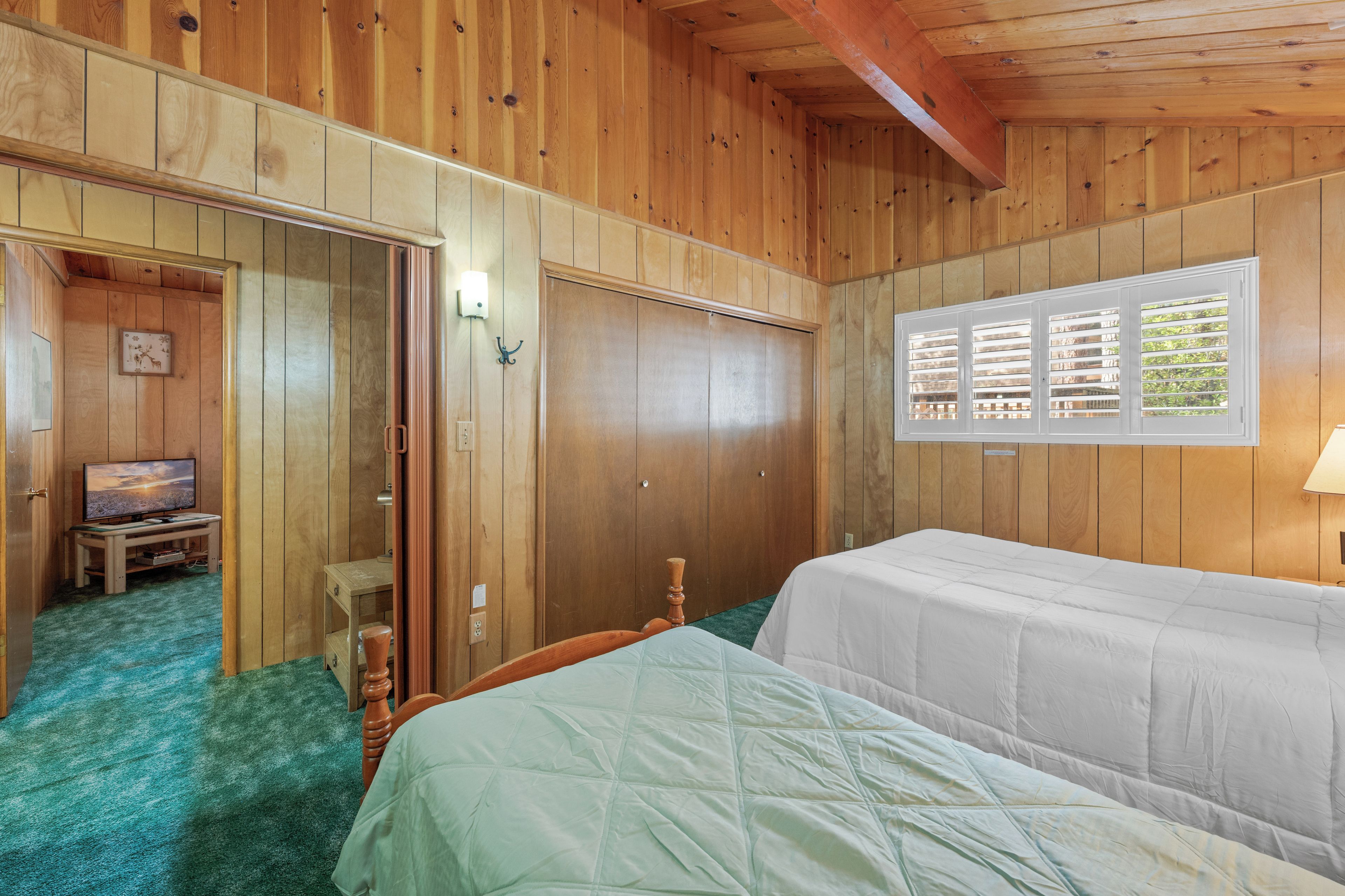 Quarto com painéis de madeira, duas camas, uma televisão e uma janela com persianas.