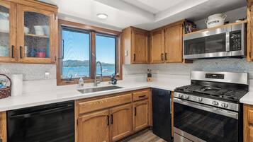 Cozinha moderna com armários de madeira, fogão de aço inoxidável, micro-ondas e uma grande janela com vista para um lago.