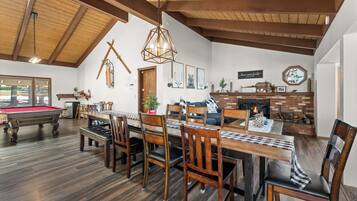 Uma ampla sala de jantar com mesa de bilhar, cadeiras de madeira e lareira de tijolos.