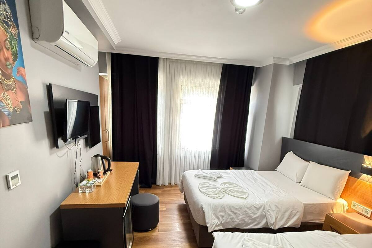 Quarto de hotel com duas camas, uma mesa, uma televisão e uma janela com cortinas.