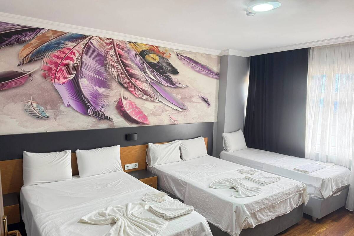 Quarto de hotel com duas camas, um mural de penas na parede e uma janela com cortinas.