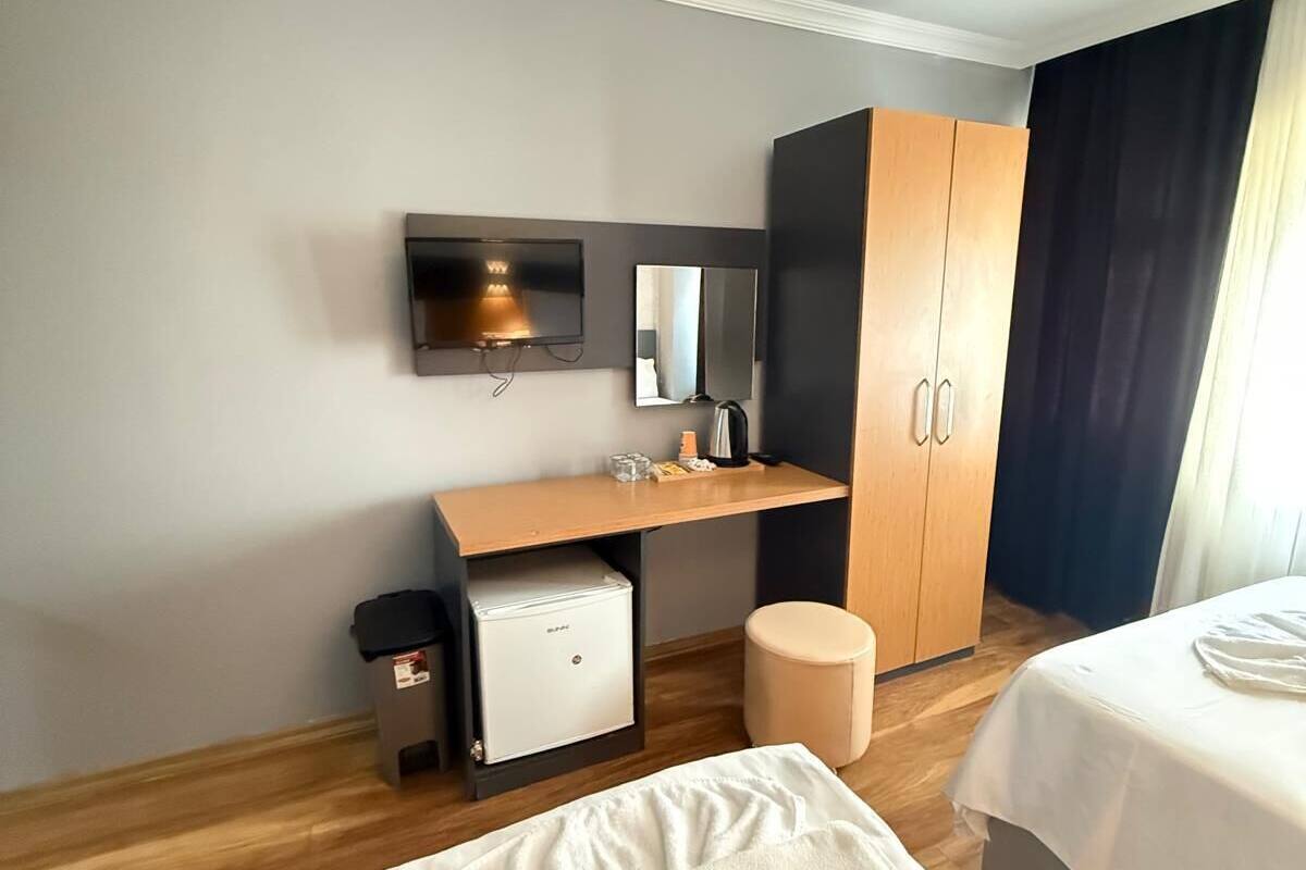 Quarto de hotel com cama, escrivaninha com computador, armário e televisão.