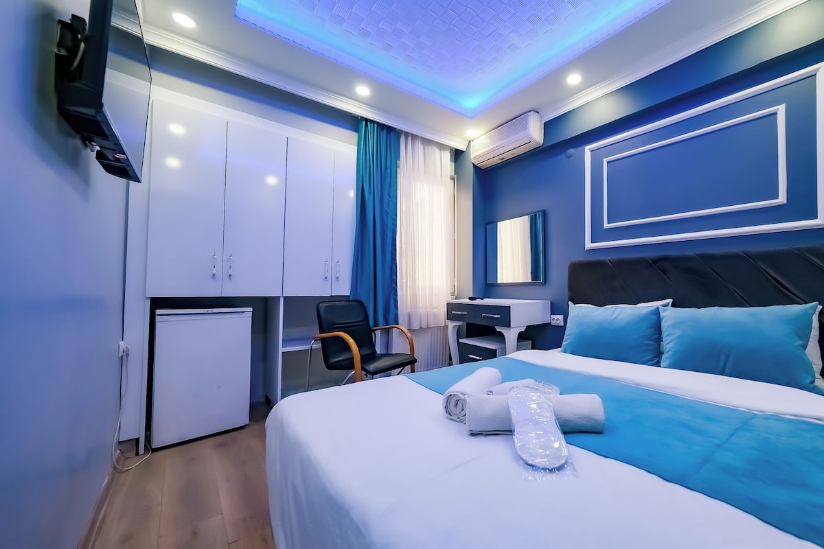 Quarto de hotel moderno com uma cama bem arrumada, uma escrivaninha e uma cadeira.
