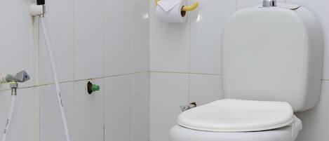 Casa de banho pequena e branca com sanita, chuveiro e suporte para toalhas.