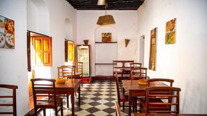 Um restaurante com mesas e cadeiras de madeira, chão xadrez e quadros nas paredes.