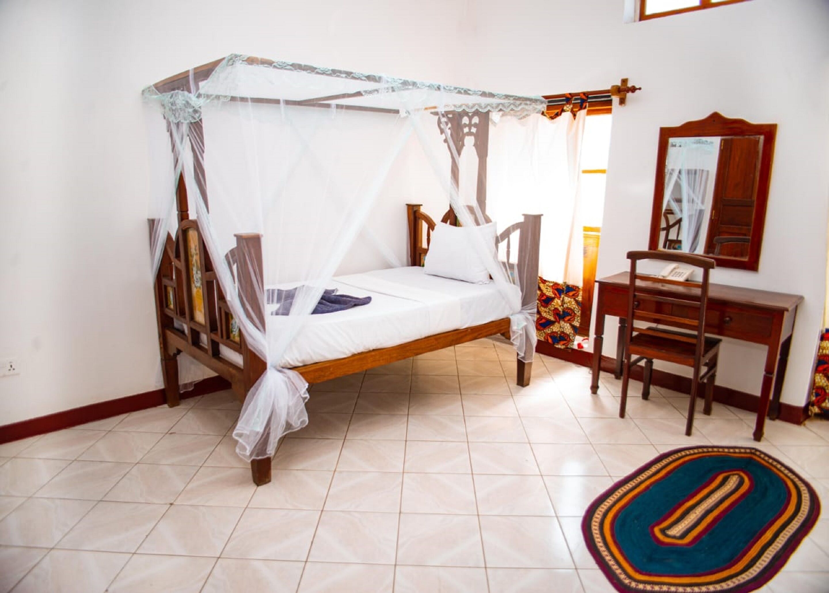 Quarto com cama sob mosquiteiro, escrivaninha de madeira e uma cadeira.
