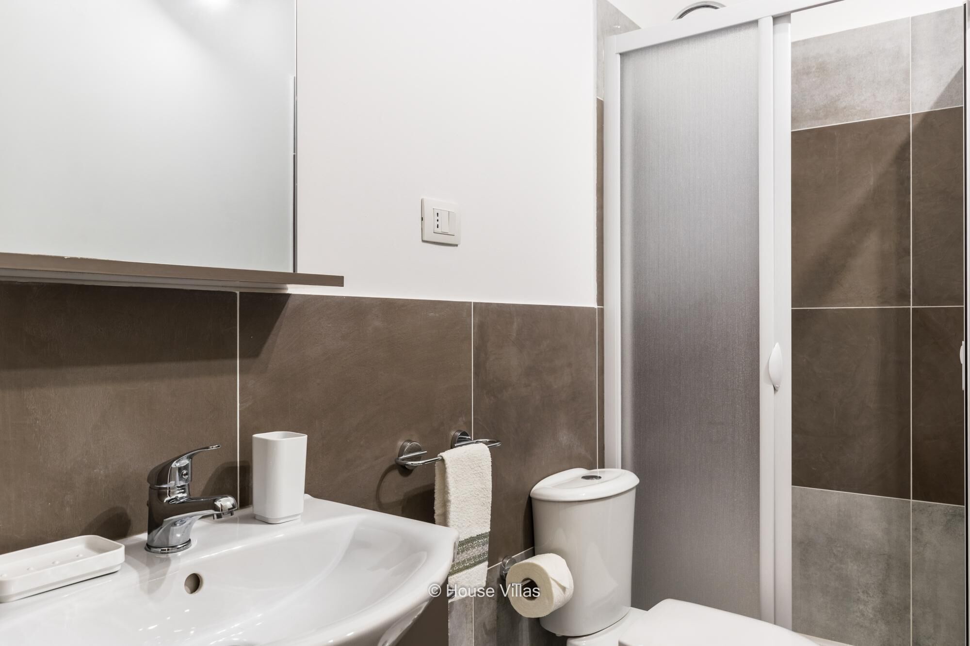 Casa de banho moderna com lavatório branco, torneira cromada e sanita com dispensador de papel.