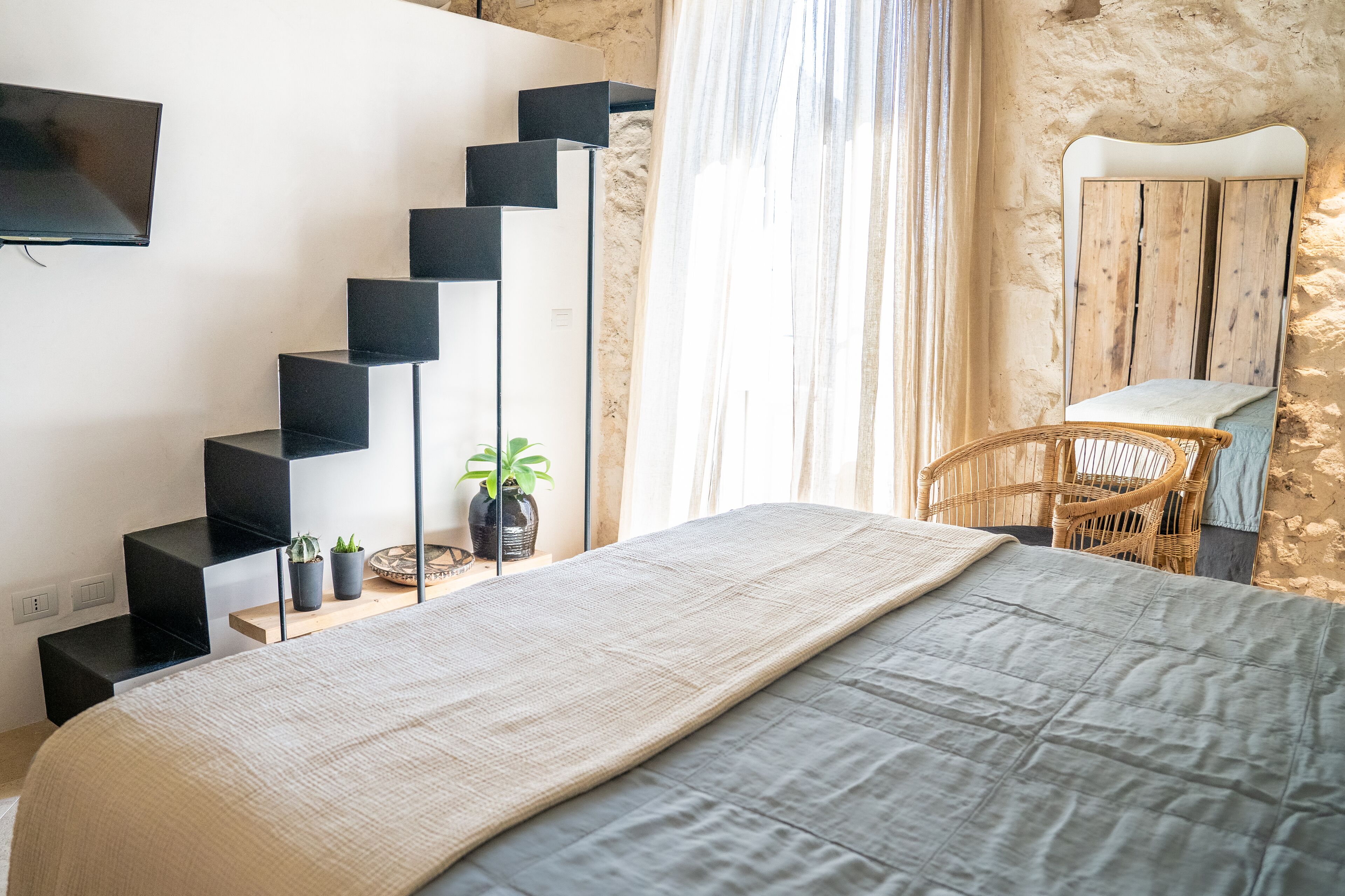 Quarto com cama, televisão fixada na parede, escada com degraus pretos e uma cadeira.
