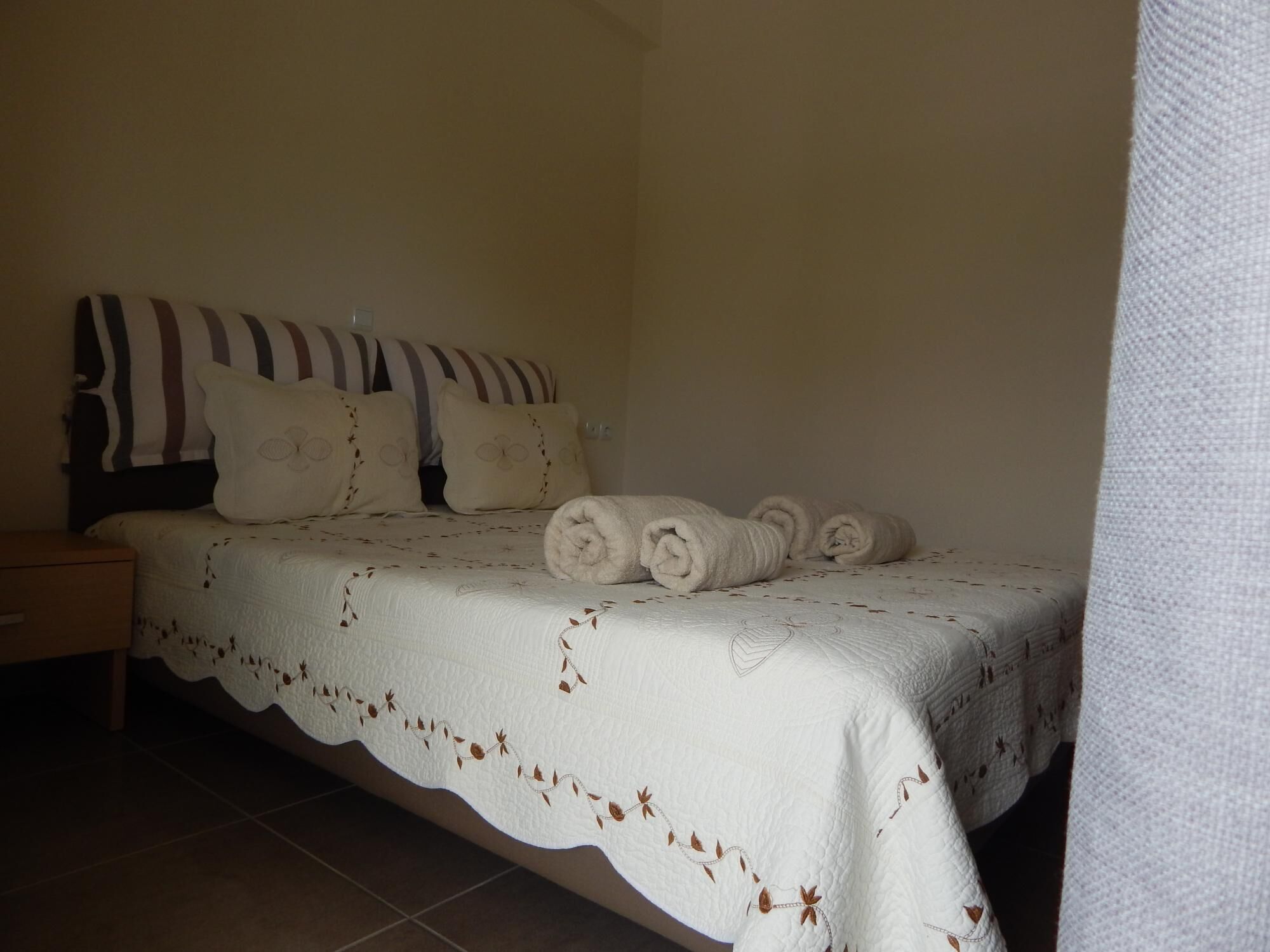 Cama arrumada com toalhas enroladas, fronha listrada e almofada estampada com flores.