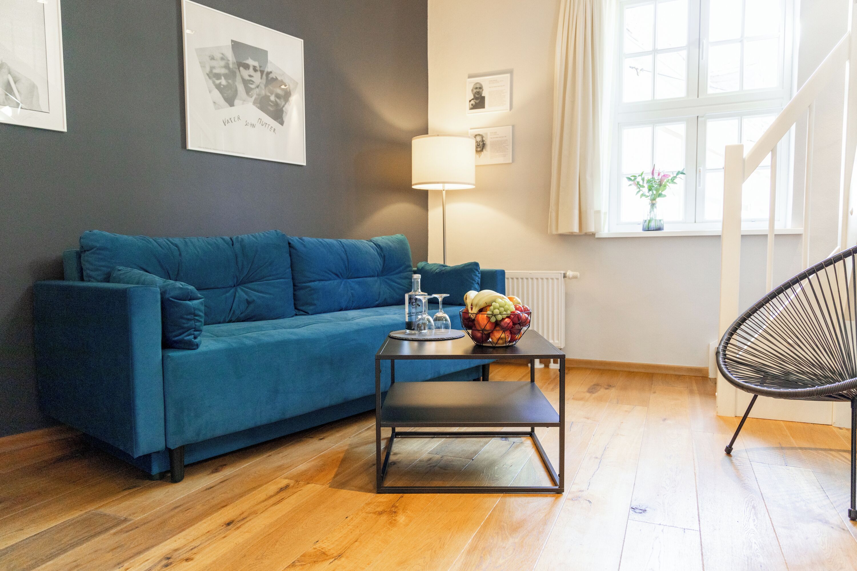 Uma sala de estar moderna com um sofá azul, uma mesa de centro com frutas e copos, uma luminária e quadros nas paredes.