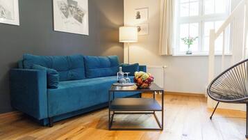 Uma sala de estar moderna com um sofá azul, uma mesa de centro com frutas e copos, uma luminária e quadros nas paredes.