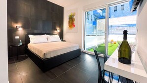 Quarto moderno com uma cama grande, uma mesinha de cabeceira, uma cadeira e uma garrafa de vinho sobre uma mesa.
