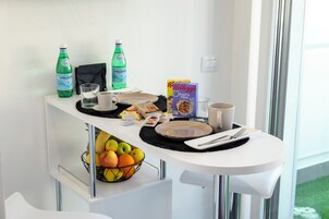 Disposição para o café da manhã com uma cesta de frutas, caixa de cereais e bebidas sobre uma mesa branca.