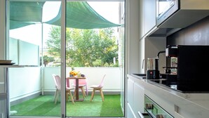 Uma cozinha moderna com área de jantar, uma porta de vidro deslizante que dá para uma varanda com grama sintética e vista para árvores e edifícios.
