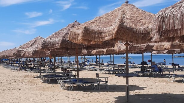 Uma praia com fileiras de guarda-sóis de palha e espreguiçadeiras.