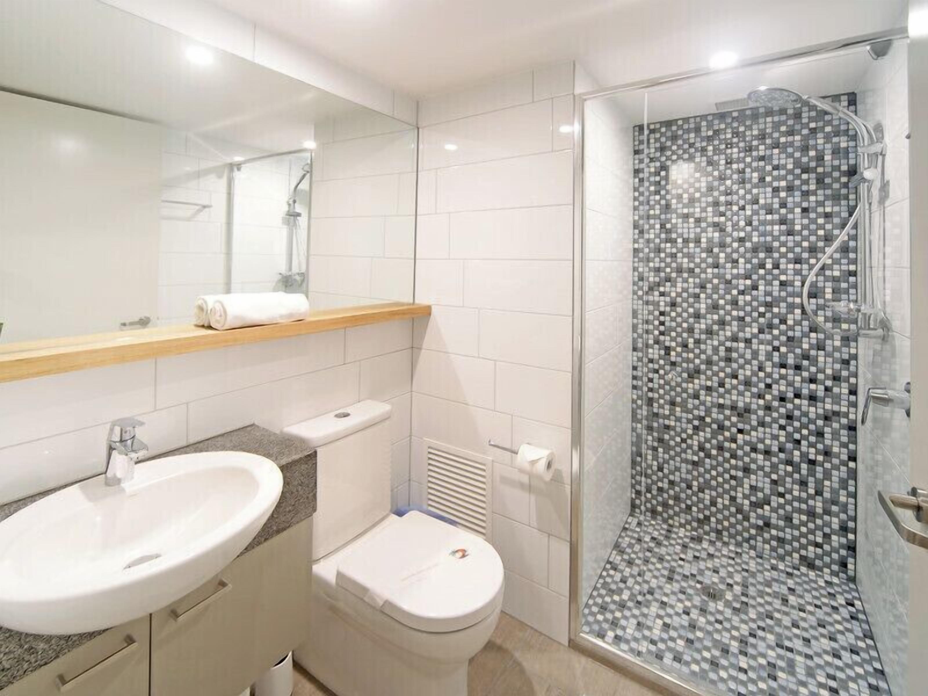 Uma casa de banho moderna com cabine de duche em vidro, uma sanita e uma pia branca.