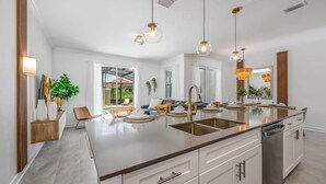 Cozinha moderna com uma ilha grande, eletrodomésticos de aço inoxidável e iluminação pendente.
