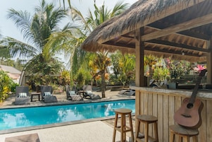 Área à beira da piscina com espreguiçadeiras, um bar e um violão.