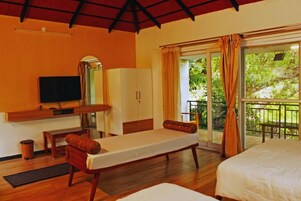 Quarto com cama, sofá, televisão e porta de vidro deslizante para uma varanda.