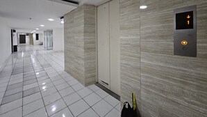 Um corredor moderno com piso ladrilhado, elevador embutido na parede e uma porta no final.