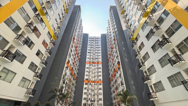 Edifício residencial alto com várias varandas, piscina central e áreas verdes ao redor.