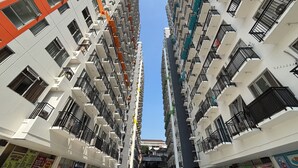 Um edifício residencial alto com várias varandas, céu claro e uma rua estreita entre os edifícios.
