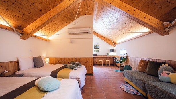 Um quarto de sótão acolhedor, com vigas de madeira, duas camas, um sofá e uma pequena cozinha.