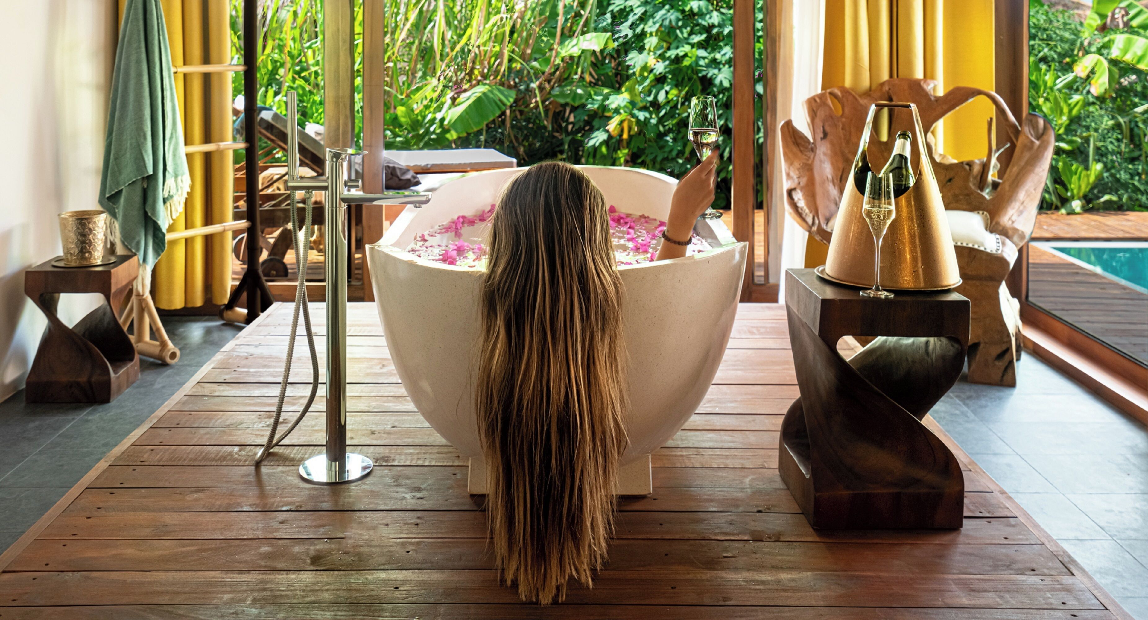 Uma banheira com pétalas de rosa, um piso de madeira e uma piscina ao fundo.