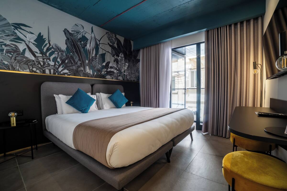 Quarto de hotel moderno com uma cama grande, uma mesa de trabalho e vista para o exterior.