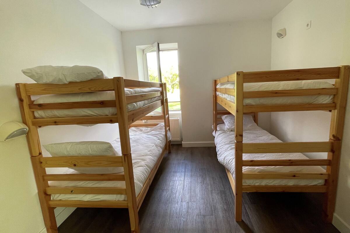 Quarto com duas beliches, um radiador e janela com vista para área verde.