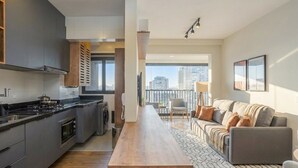Uma cozinha moderna com uma ilha central, uma área de jantar com uma mesa comprida e uma sala de estar com sofá e vista para a cidade.