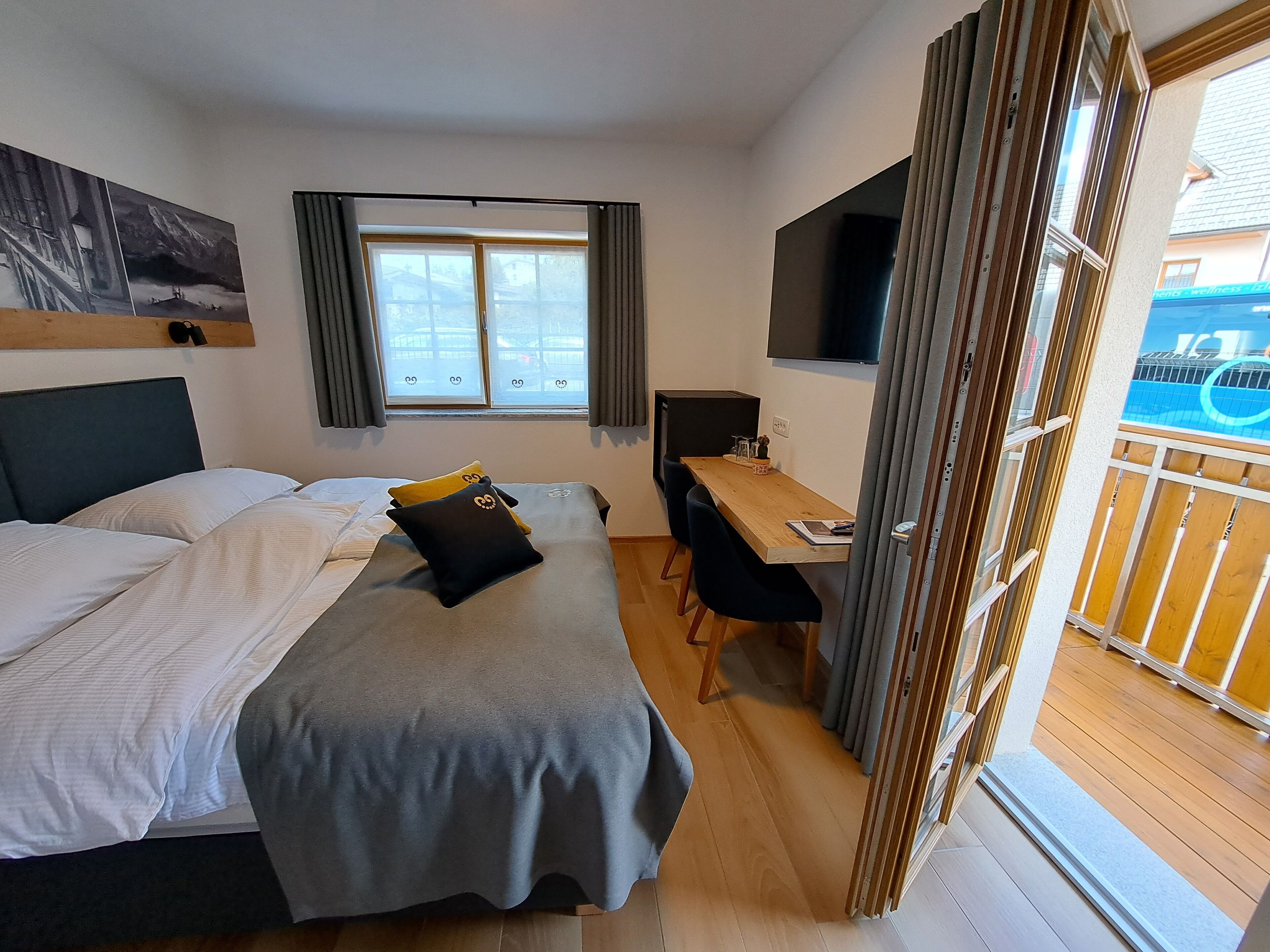 Quarto de hotel com cama, escrivaninha, cadeira, televisão e janela com cortinas.