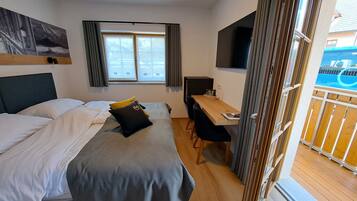 Quarto de hotel com cama, escrivaninha, cadeira, televisão e janela com cortinas.