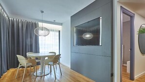 Uma zona de refeições moderna com uma mesa redonda e cadeiras, uma luminária pendente e uma grande obra de arte emoldurada na parede.