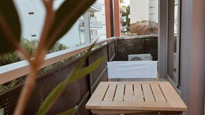 Uma varanda com mesa e cadeiras de madeira, grade de tela e vista para edifícios ao fundo.