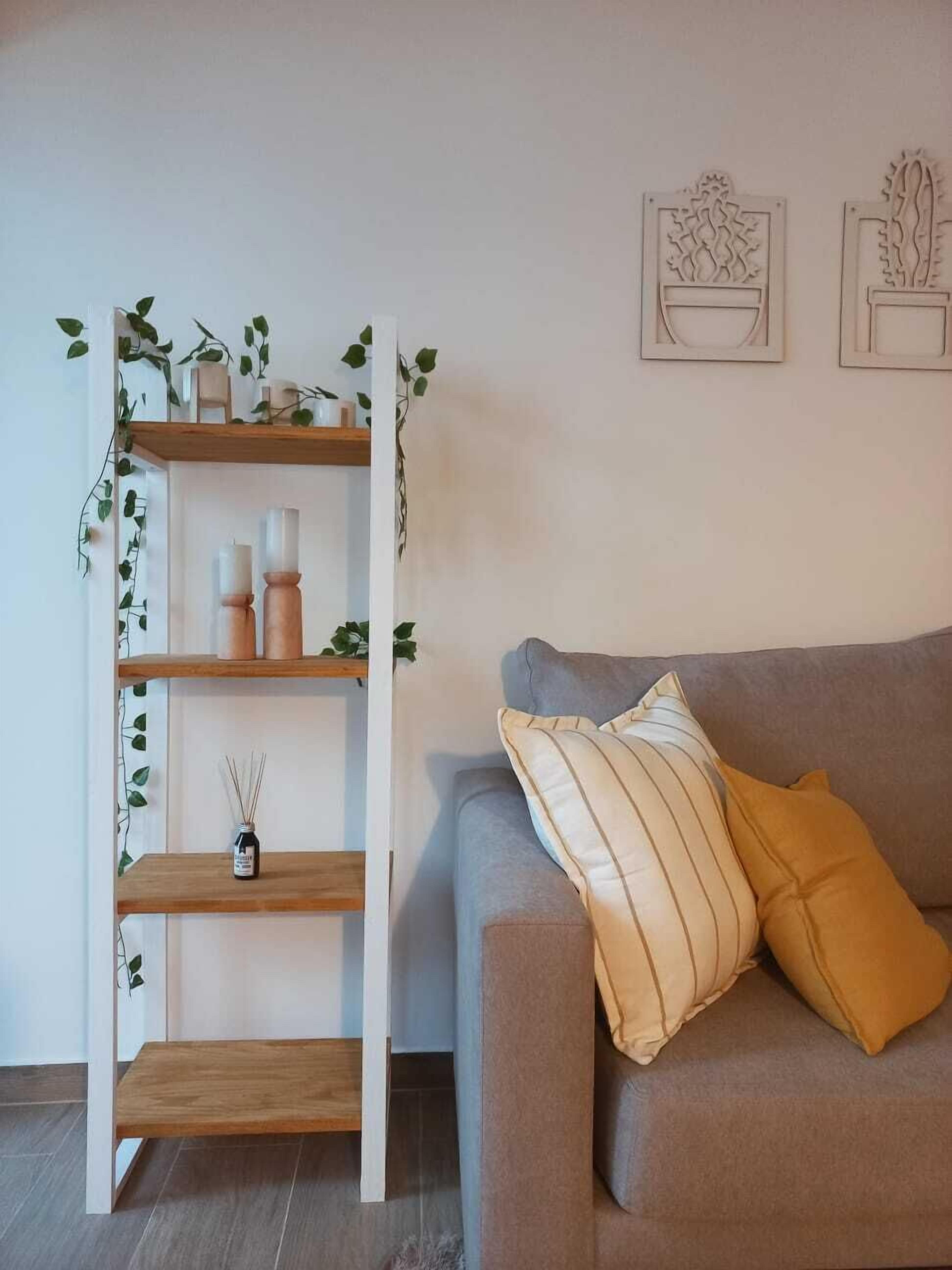 Sala de estar com sofá cinza, dois almofados, estante de madeira com velas e um frasco, e arte na parede.