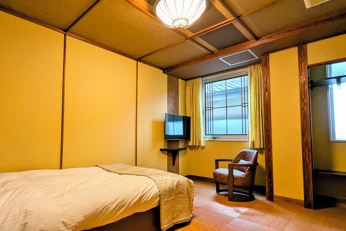 Quarto com cama, cadeira, televisão e janela com cortinas.