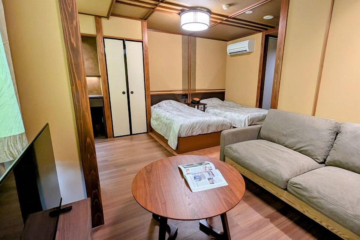 Quarto de hotel com cama, sofá, mesinha de centro com uma revista e televisão.