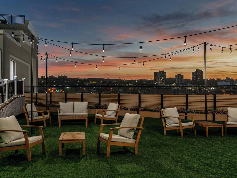 Terraço no telhado com área de estar externa e luzes de Natal, com o horizonte da cidade ao fundo ao pôr do sol.